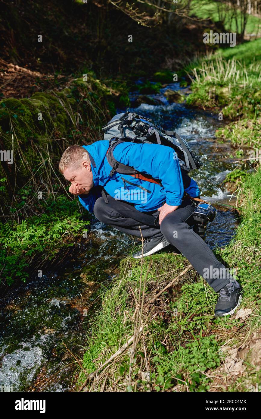 Hiker drinking stream water in mountain. Adult man drinking water from ...