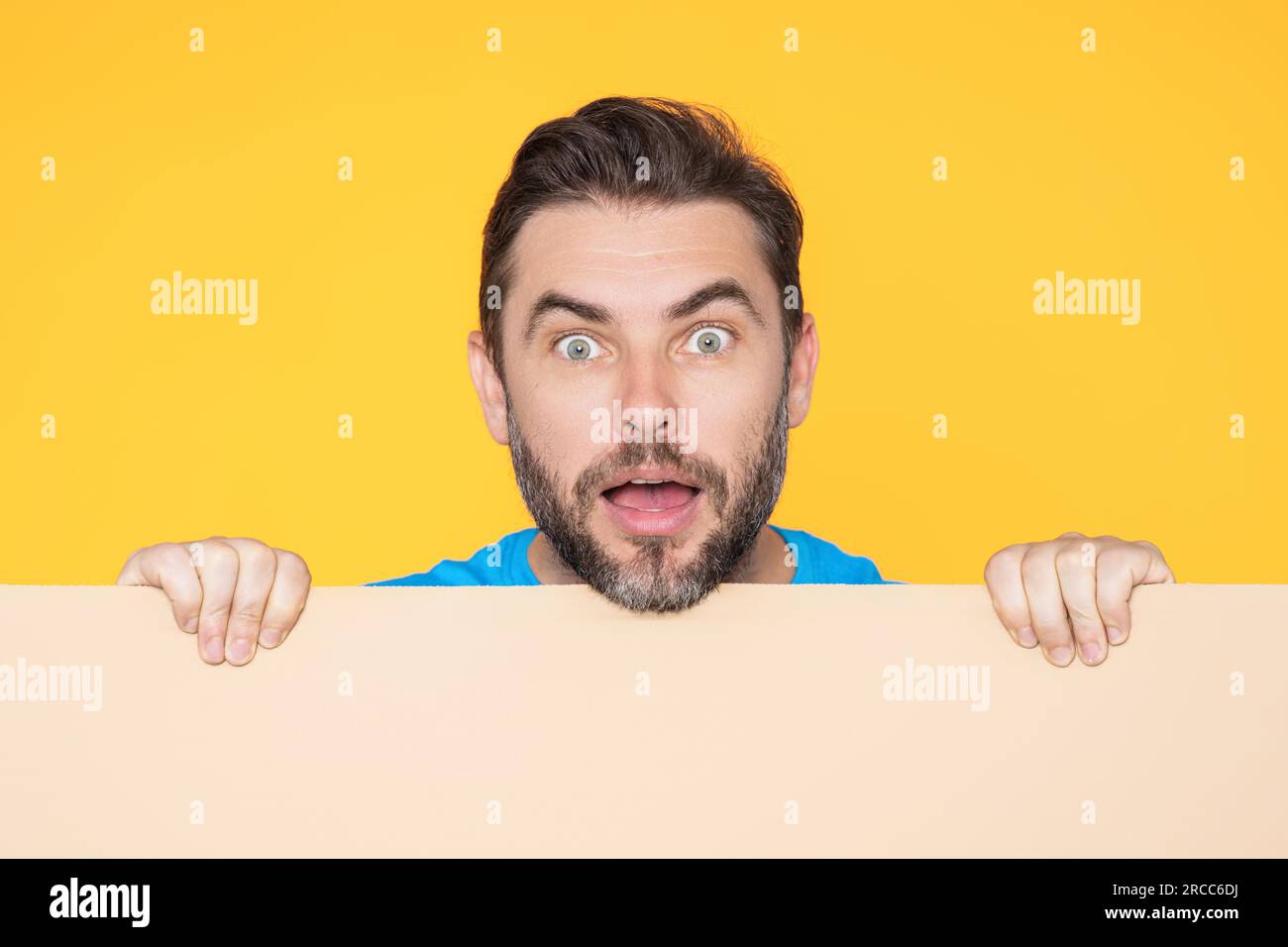 Amazed guy with blank banner ad isolated on studio background. Portrait of surprised man holding ...