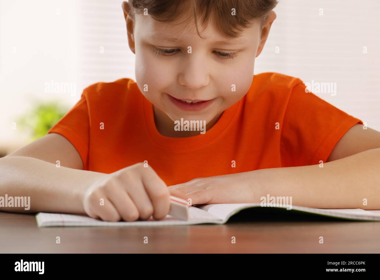 Little boy erasing mistake in his notebook at wooden desk Stock Photo ...