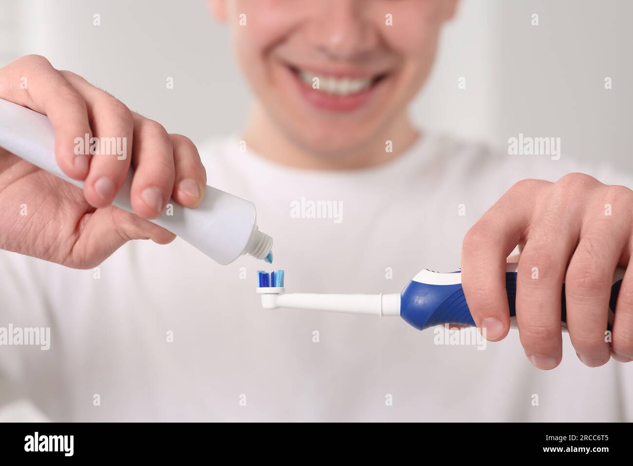 Man squeezing toothpaste from tube onto electric toothbrush on blurred ...