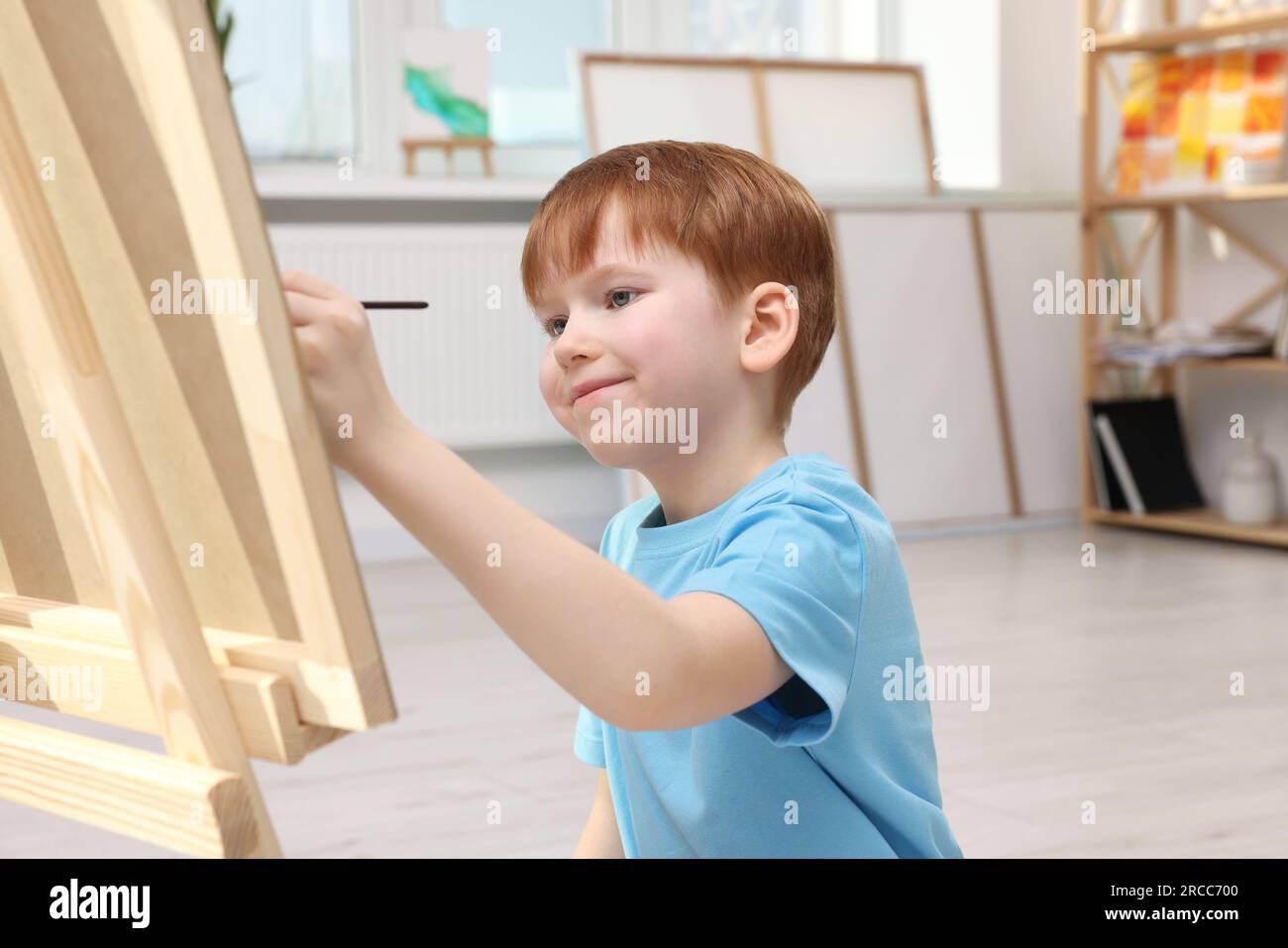 Little boy painting in studio. Using easel to hold canvas Stock Photo ...