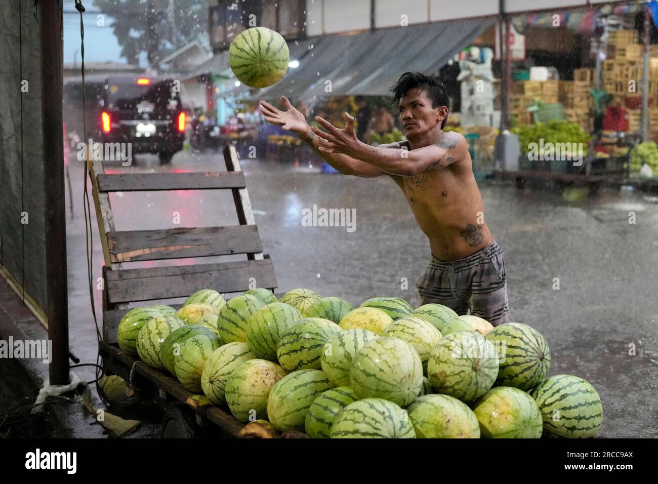 A worker catches watermelons during a downpour at a fruit market in ...