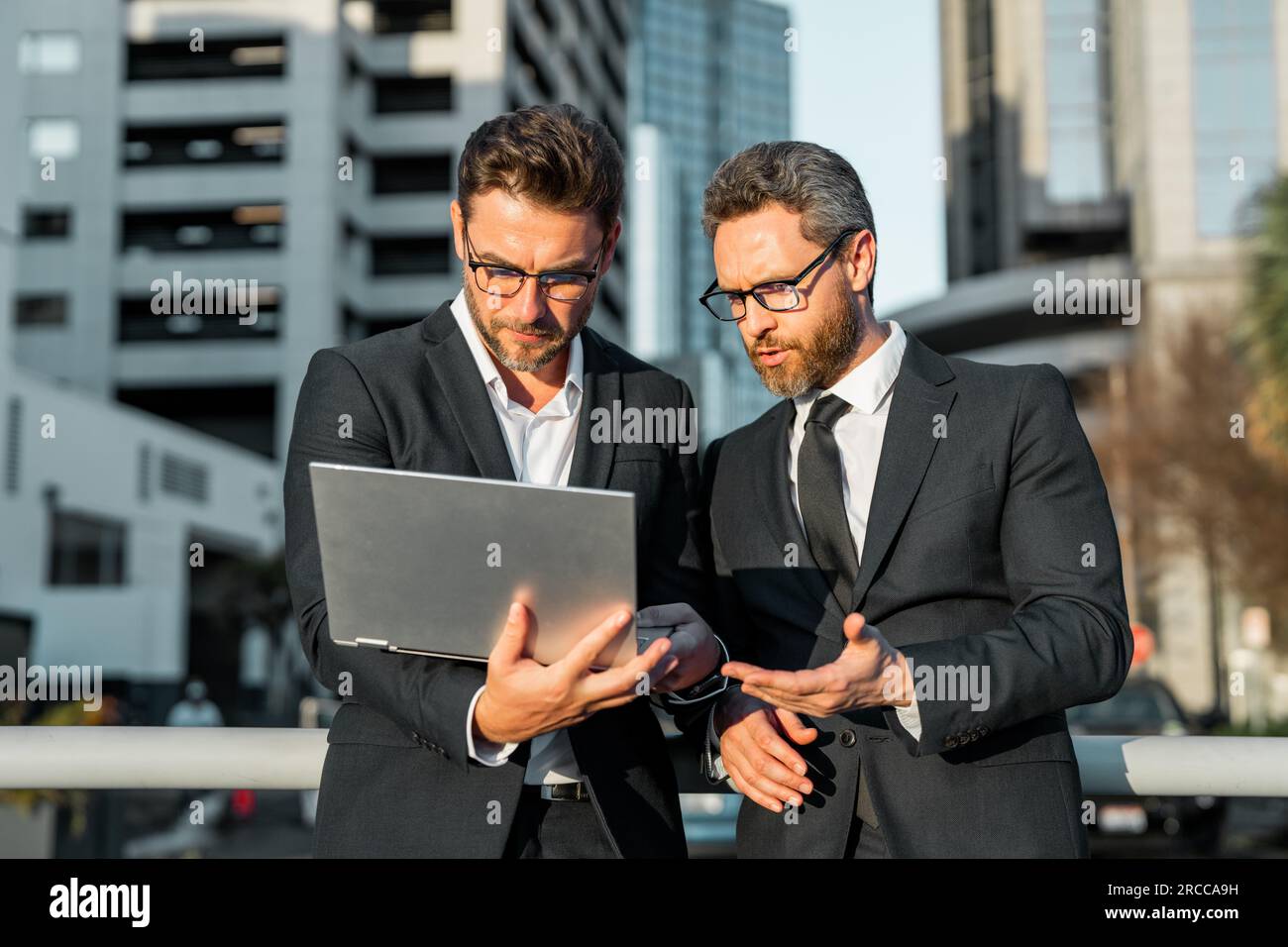 Two handsome young businessmen in classic suits using laptop ...