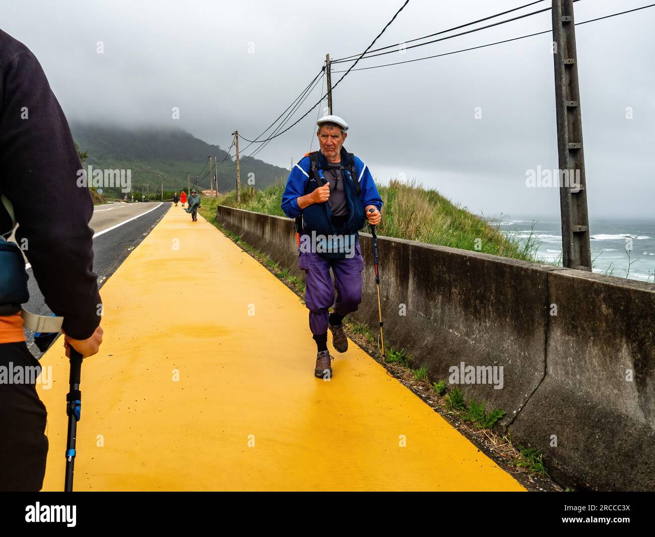 Pilgrims are seen walking on yellow pavement. The Coastal Route of the ...