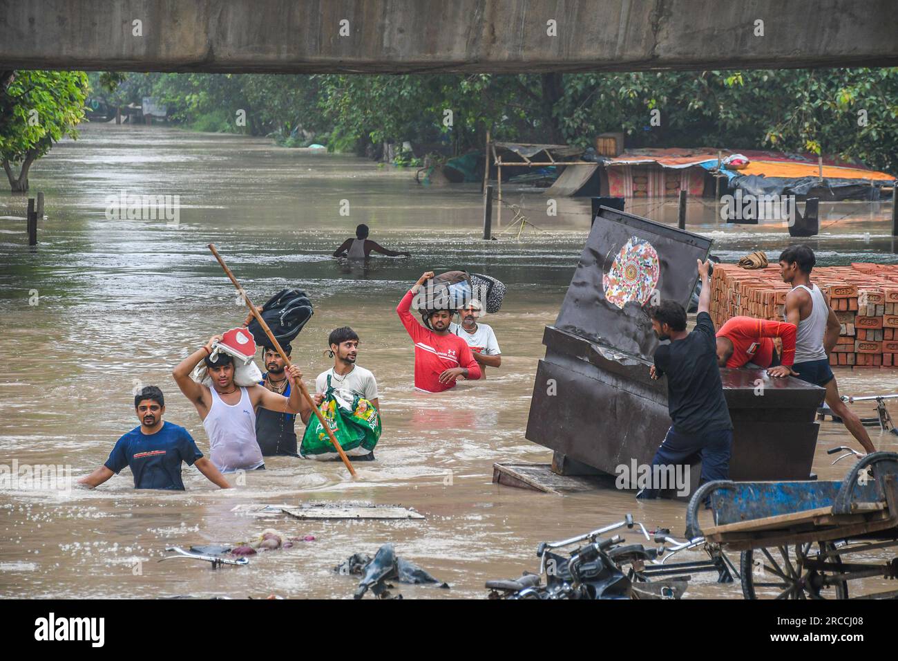 New Delhi, India. 12th July, 2023. People carry their belongings as they wade through flooded ...