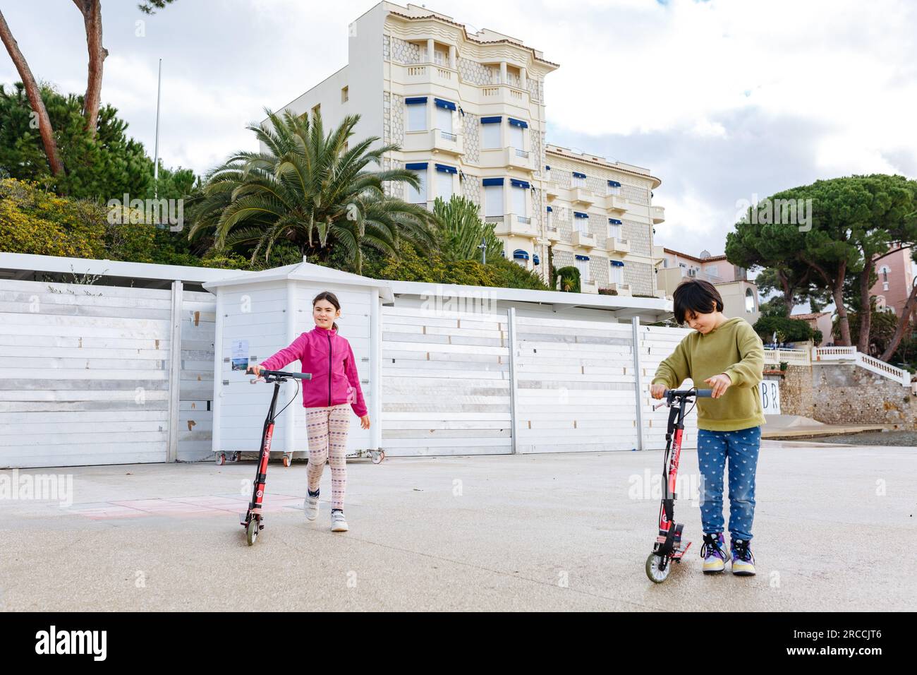 two children girls in bright casual clothes riding red scooters next to ...
