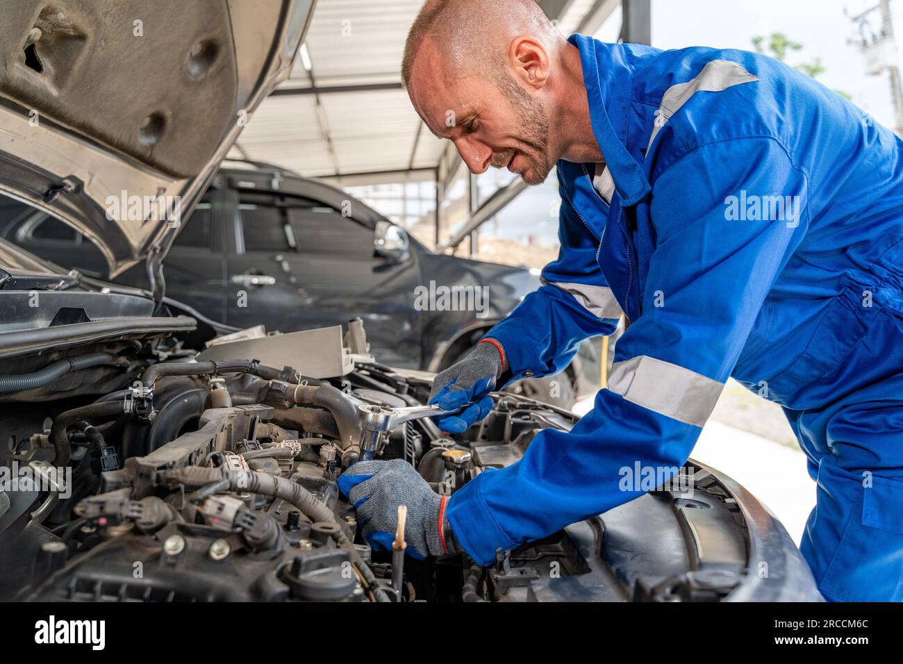A male car mechanic in blue jumpsuit working hard to repair the car ...