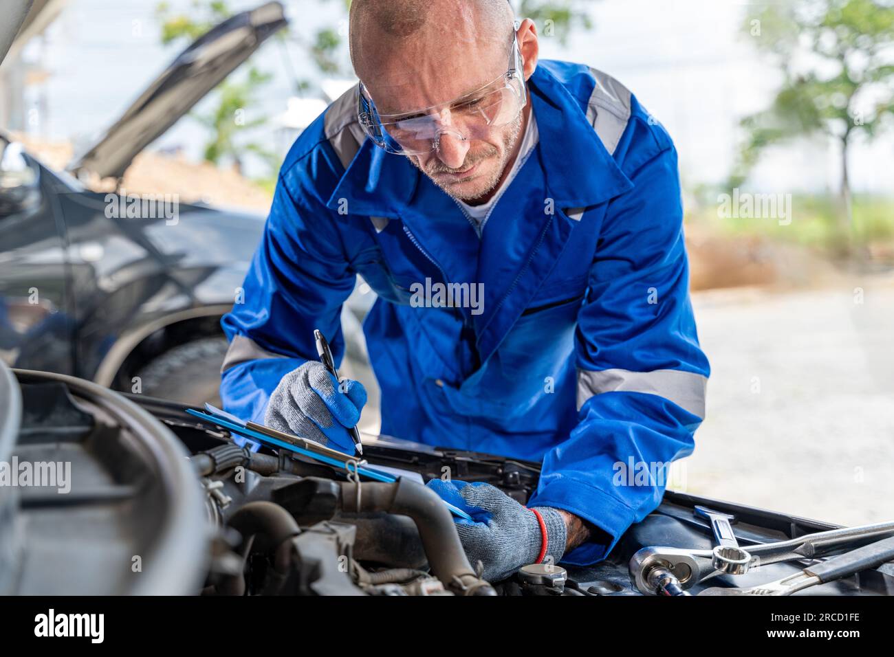 A male car mechanic taking notes for the car repair on his paper ...