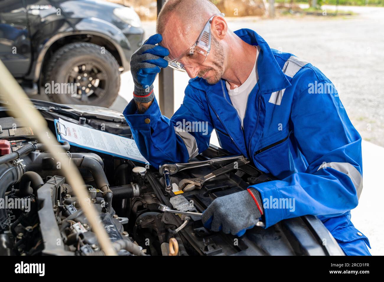 A male car mechanic wearing eye protection goggles in blue jumpsuit ...