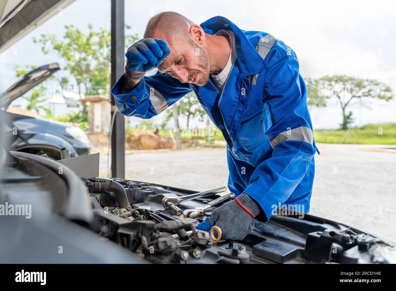 A tired male car mechanic in jumpsuit wiping off his sweat from his ...