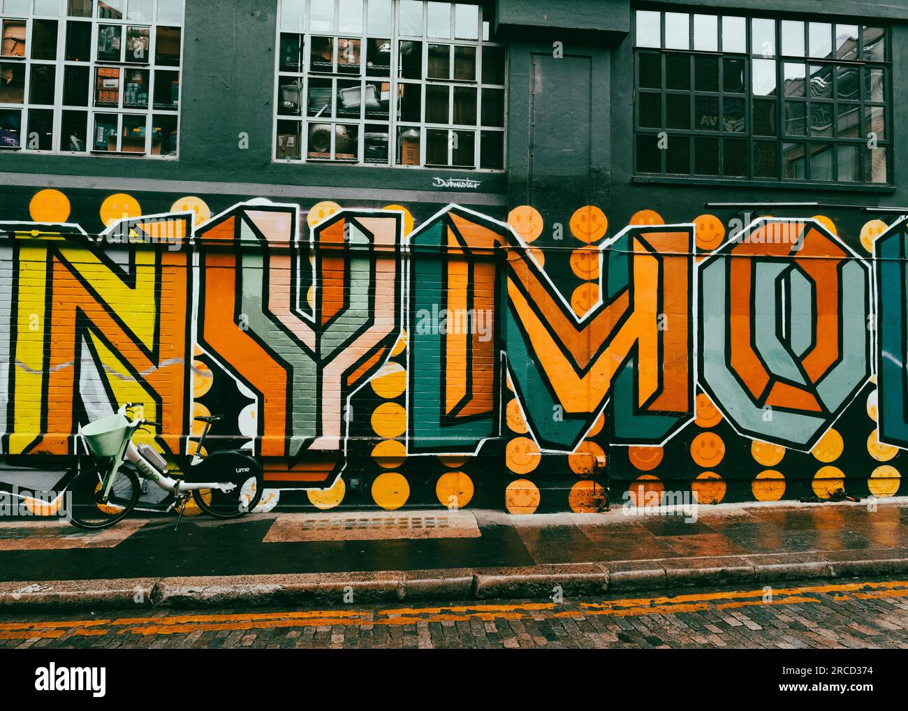 A bicycle resting by graffiti on buildings on a wet Saturday morning in ...