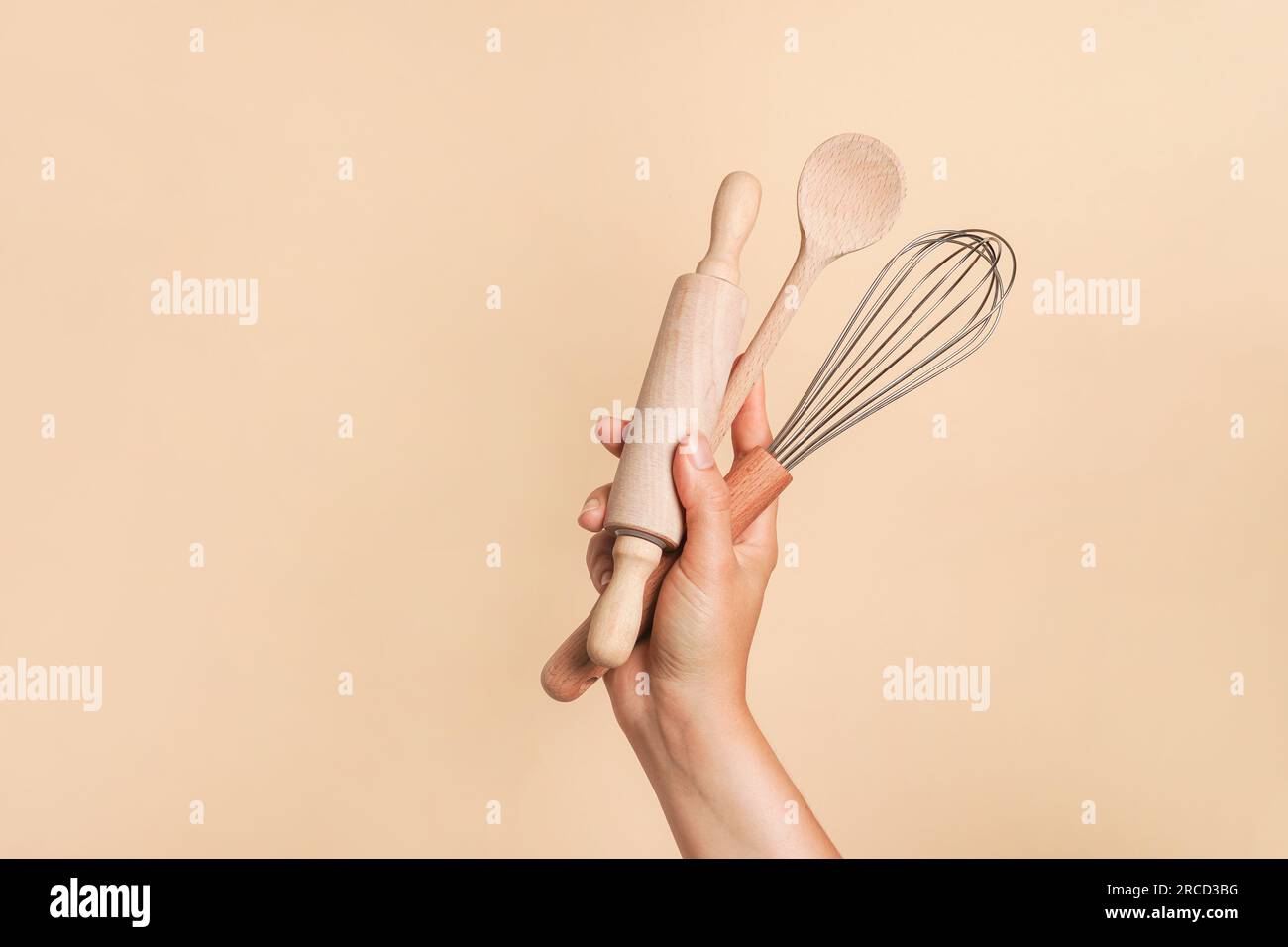 Female hand holding kitchen utensils for food and bakery on beige ...