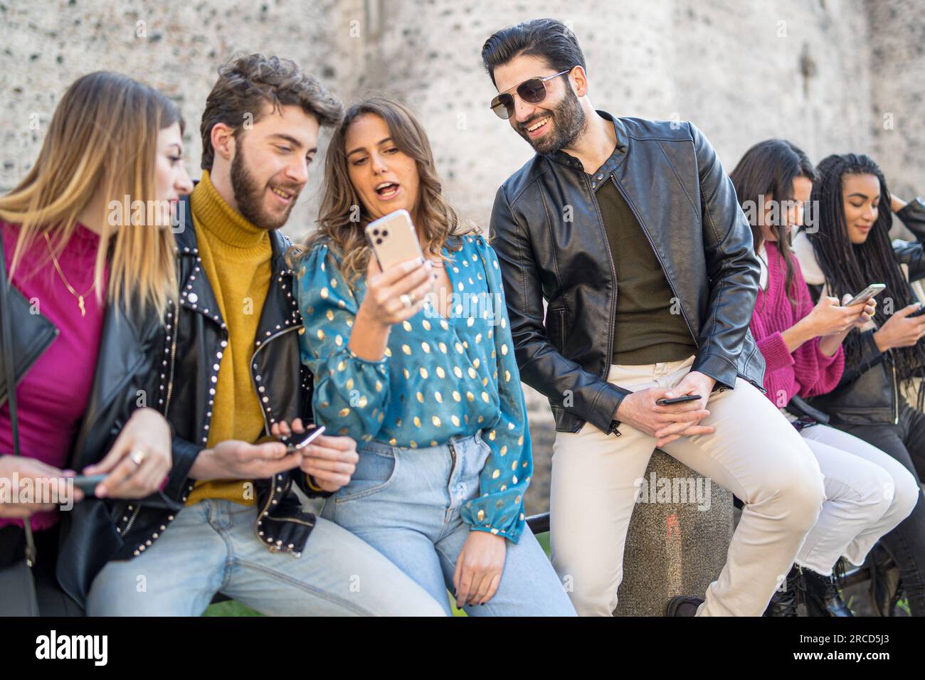 A group of friends sitting on a railing outdoors, laughing, joking, and ...