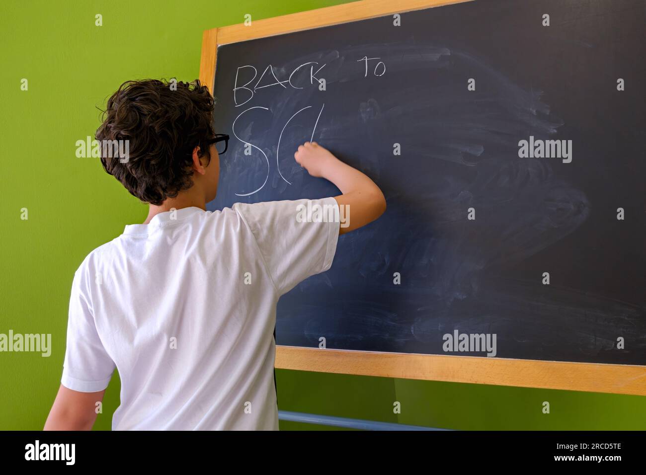 Back view of a young schoolboy writing 'Back to School' with white ...