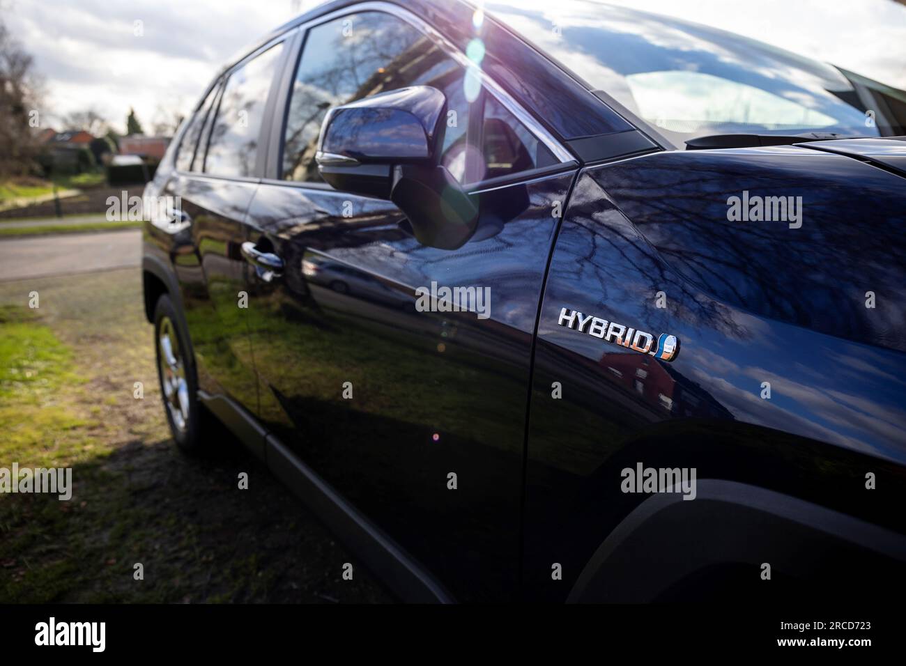 A portrait of the side of a dark blue car, with an hybrid emblem on the ...