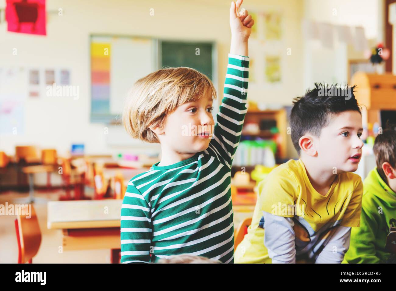 Two concentrated 4-5 year old boys in classroom, kid raising hand on ...