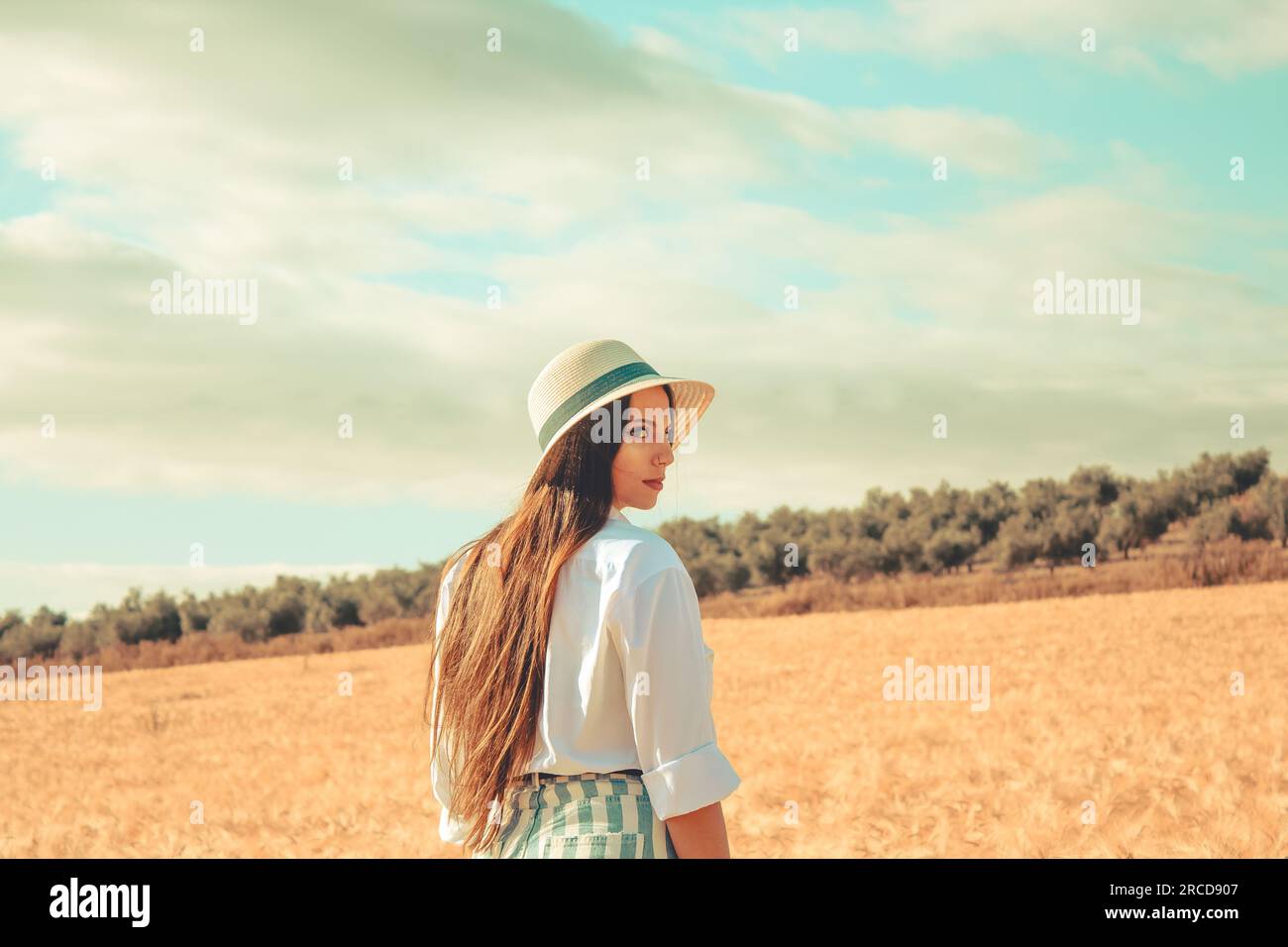 A young girl walking through a wheat field during a sunny spring day ...