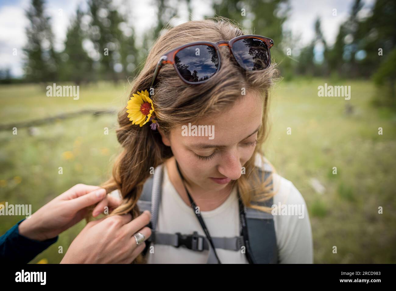 Closeup of young women with flower in hair being braided in nature ...