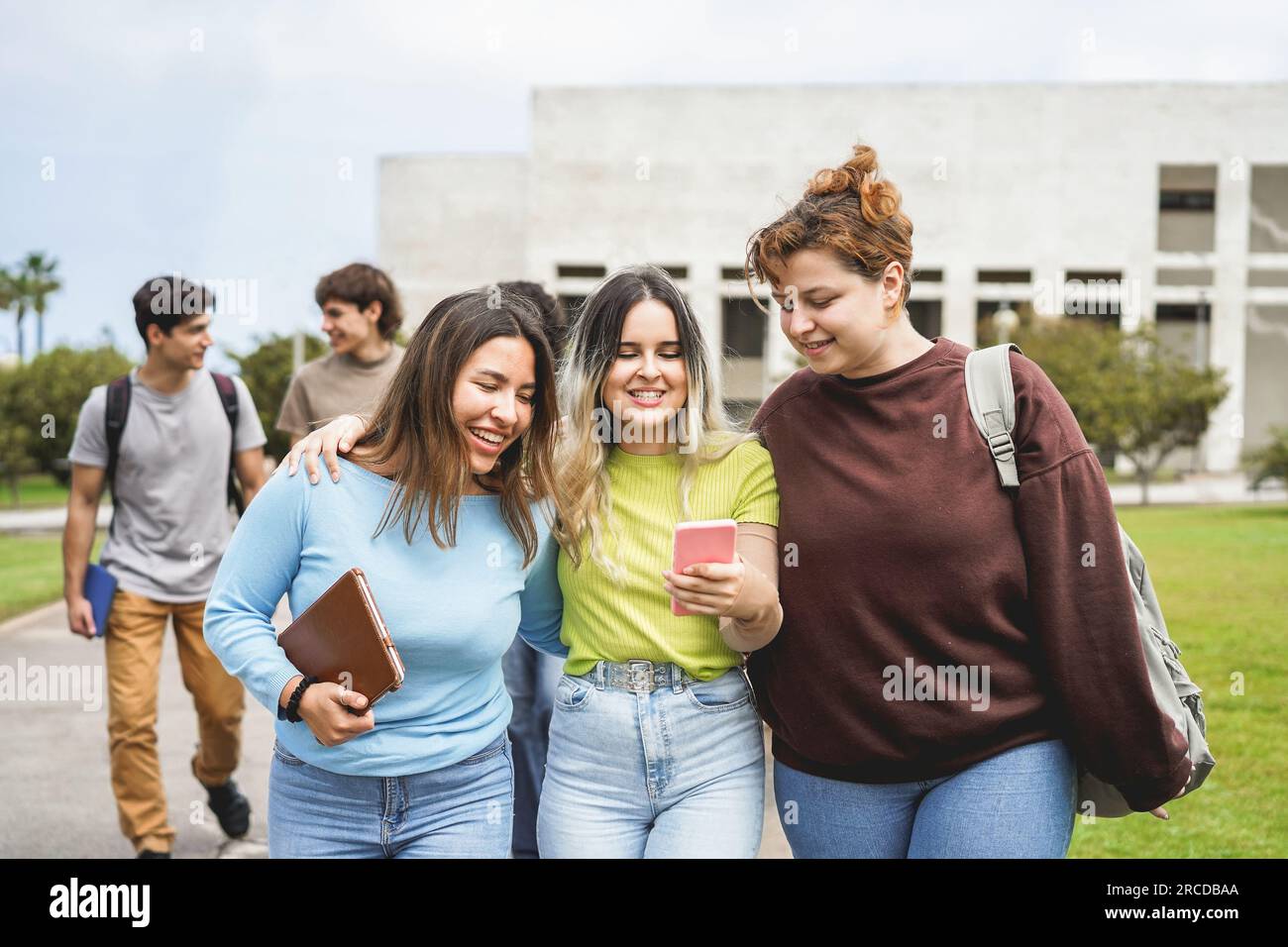 Young group of students having fun outdoor using smartphone while going ...