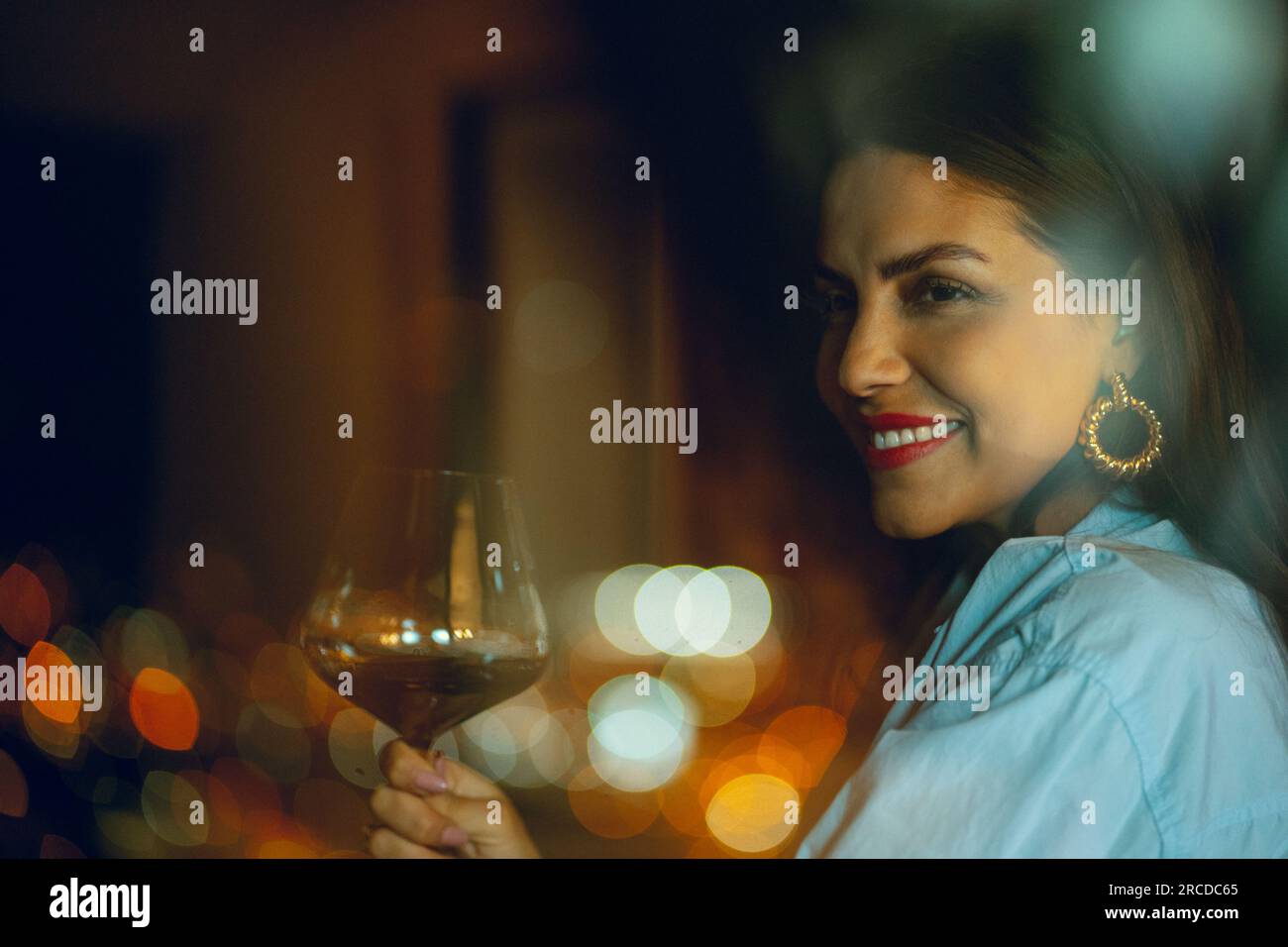 Beautiful woman with a glass of wine smiling through a window view ...