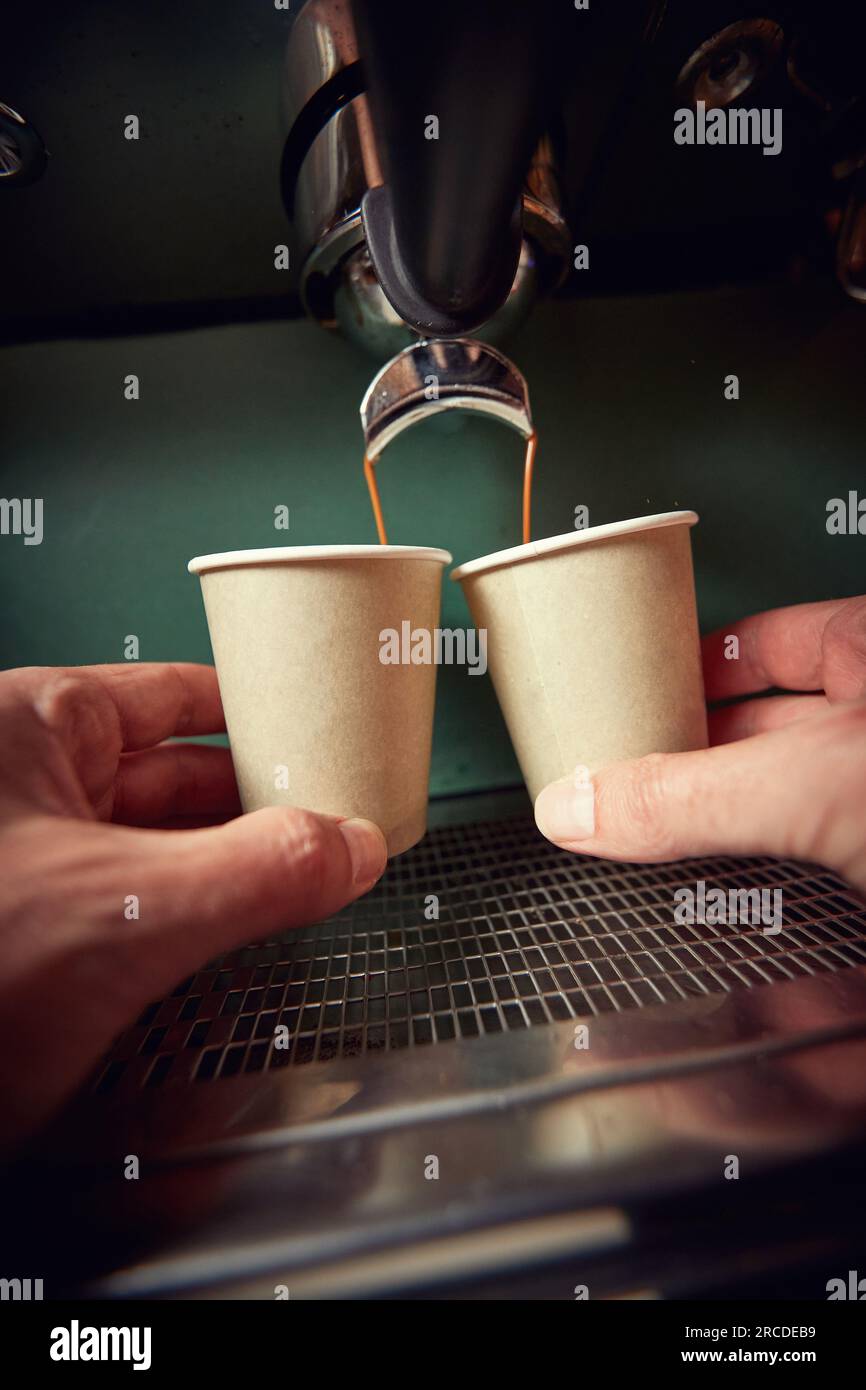 caucasian male hands holding two paper cups below the jet of black ...