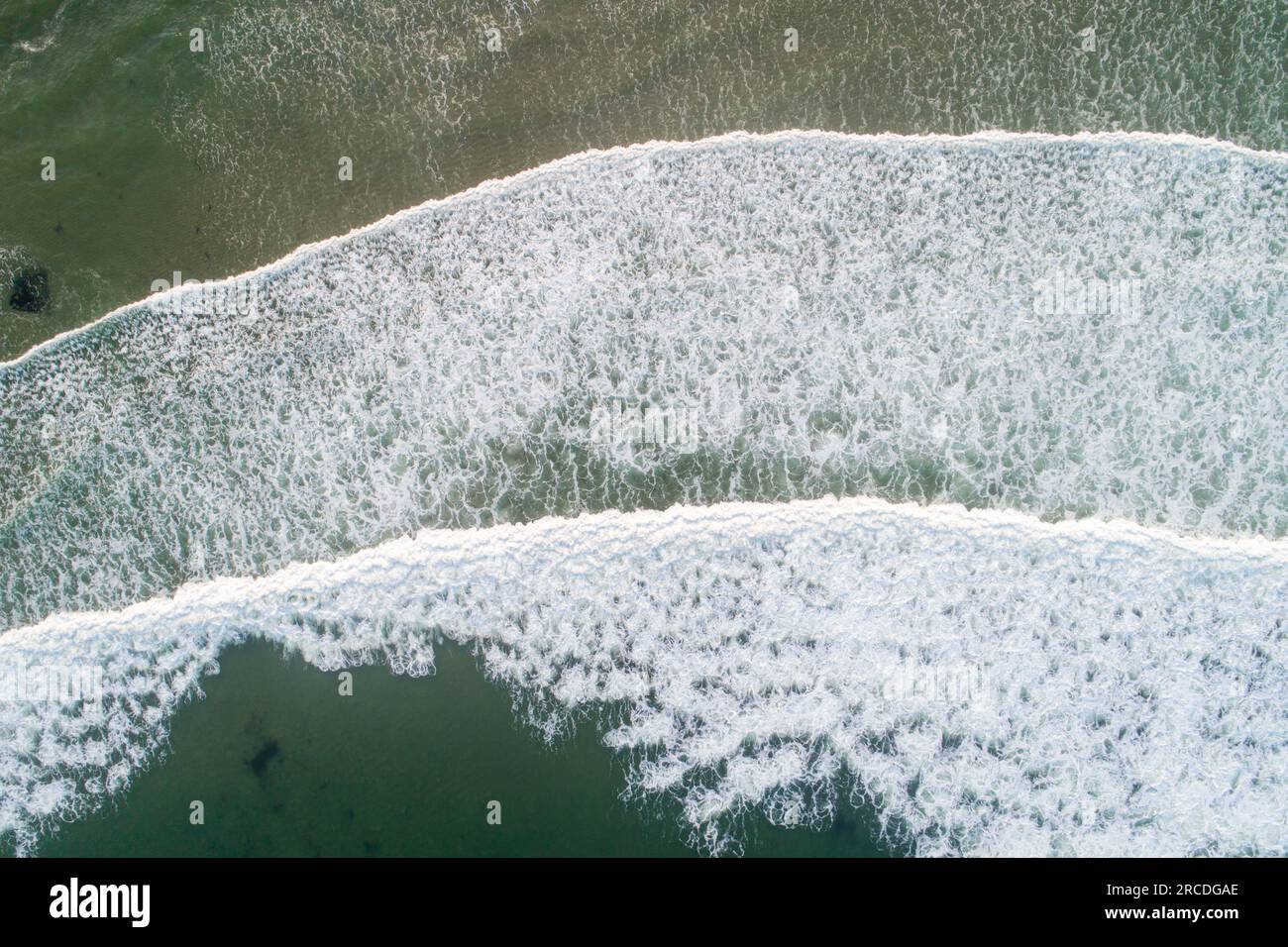 Aerial view of turquoise ocean creating patterns in the sand at sunset ...