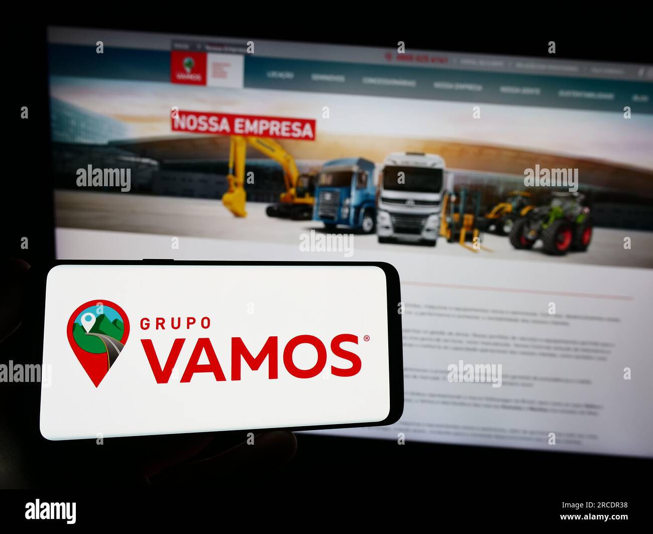 Person holding smartphone with logo of Brazilian truck rental company Grupo Vamos on screen in ...