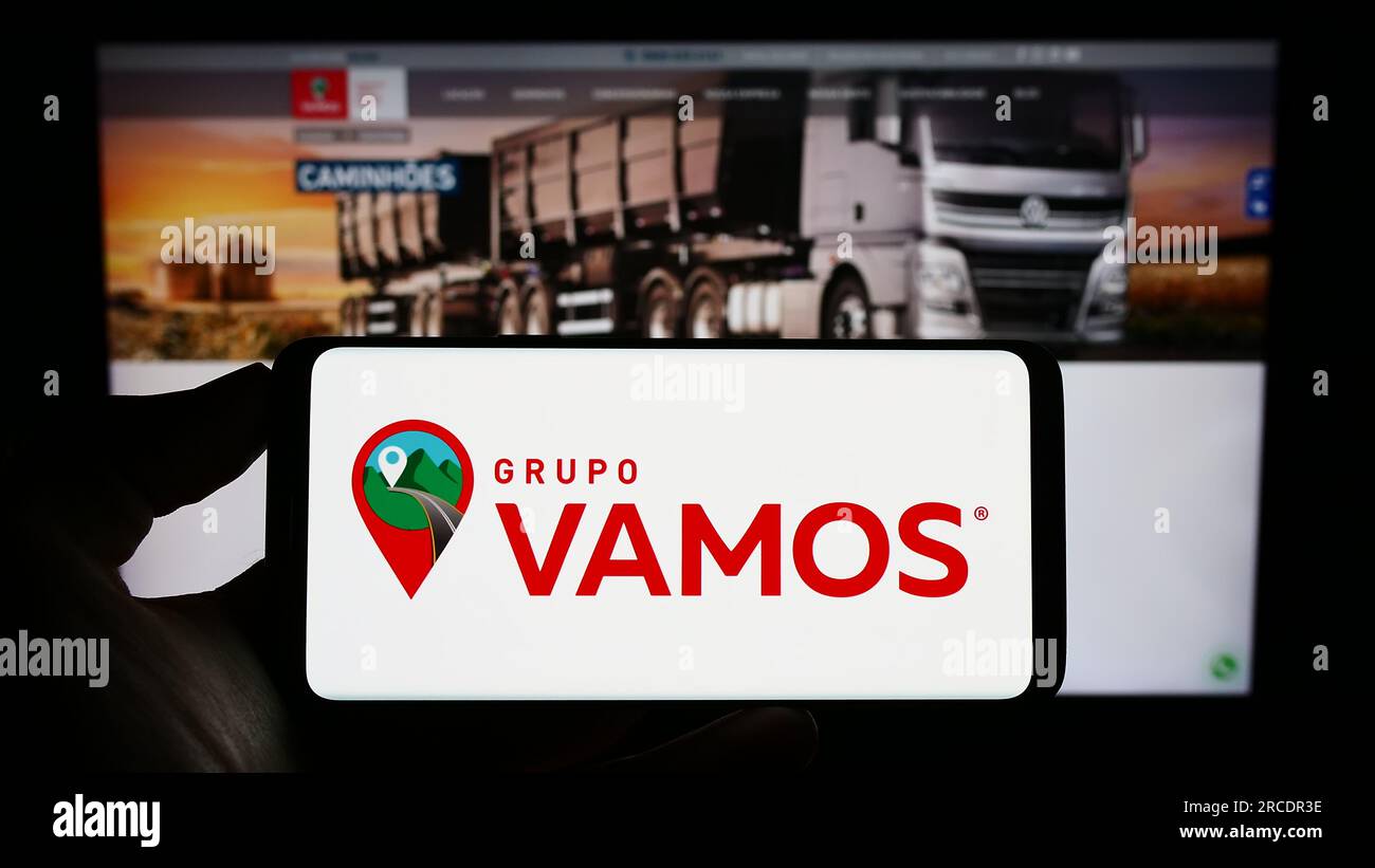 Person holding mobile phone with logo of Brazilian truck rental company Grupo Vamos on screen in ...