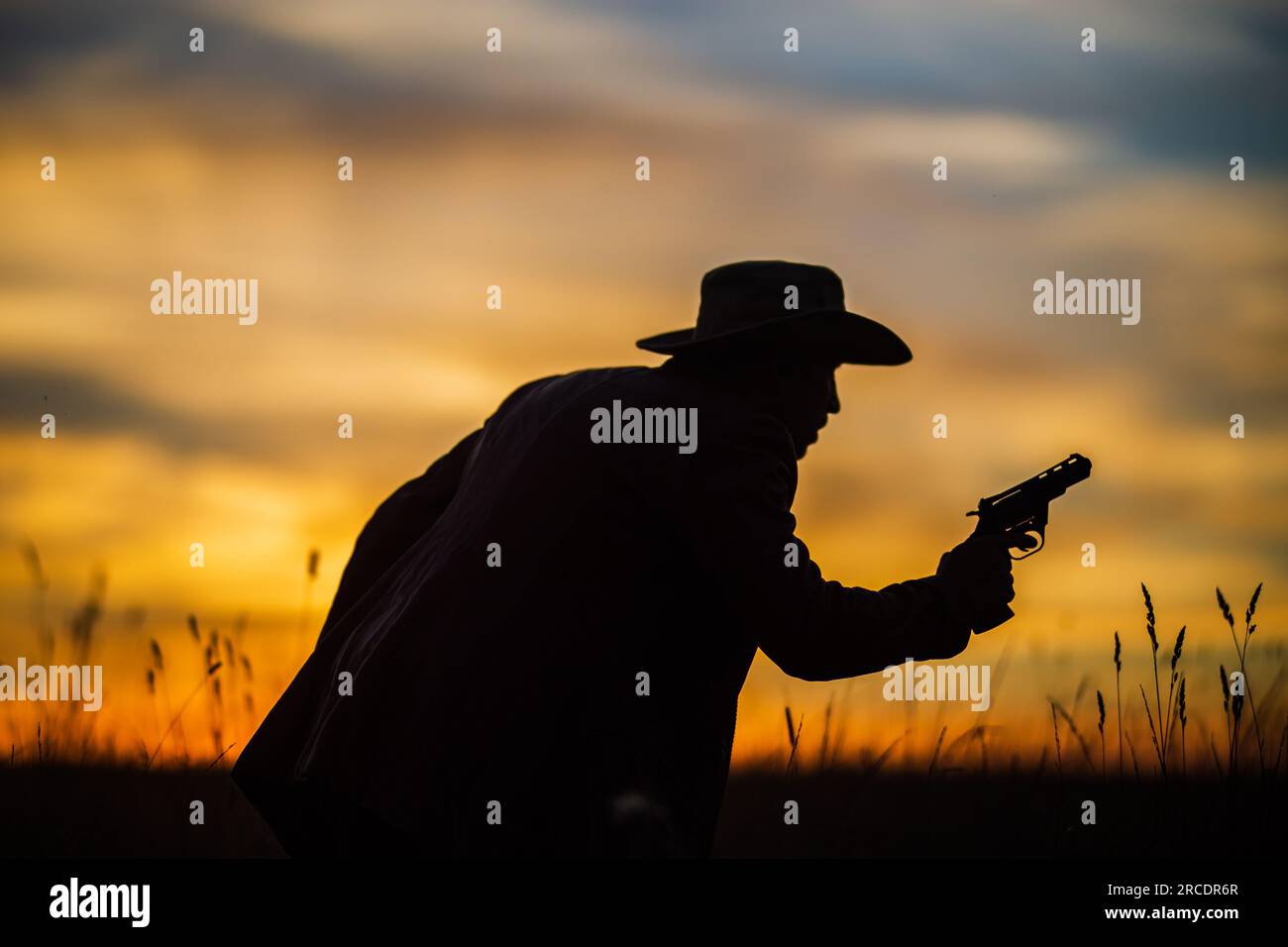 Silhouette of a cowboy in a hat with a revolver against a dramatic ...
