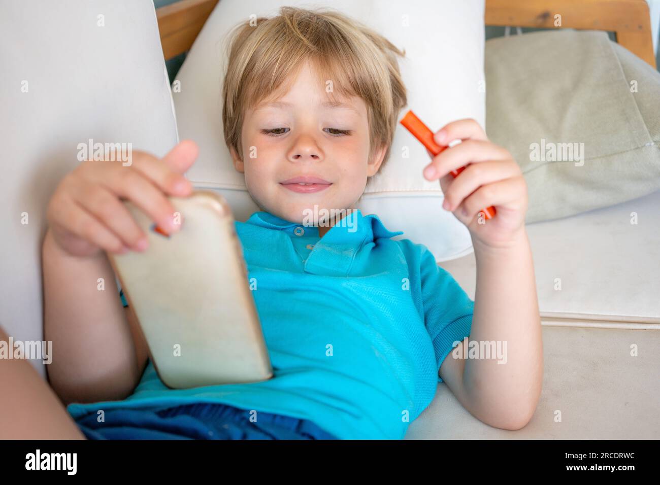 Cute little boy using smartphone, lying on cozy couch, relaxing on ...