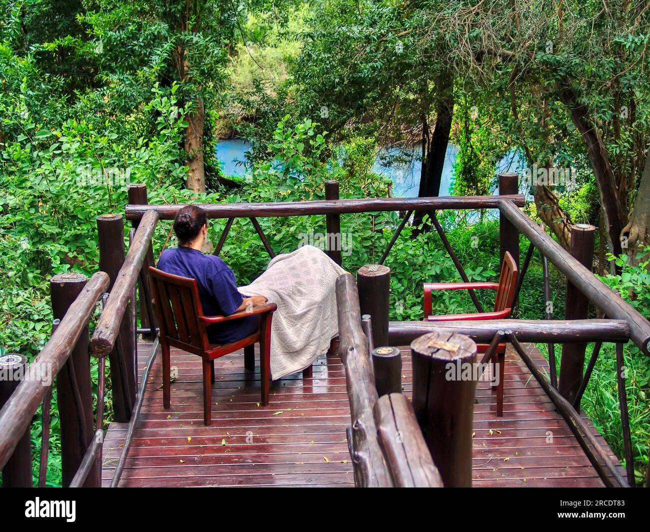 elderly woman relaxing on a wooden chair on the terrace next to te ...