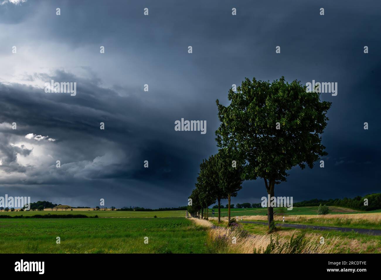 A storm moves over the field and the country road with the tree-lined ...