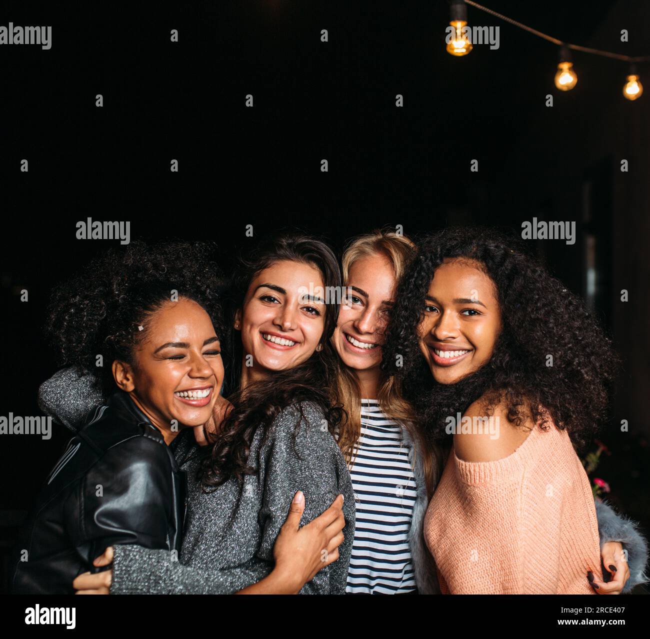 Group of four laughing female friends embracing at night Stock Photo ...