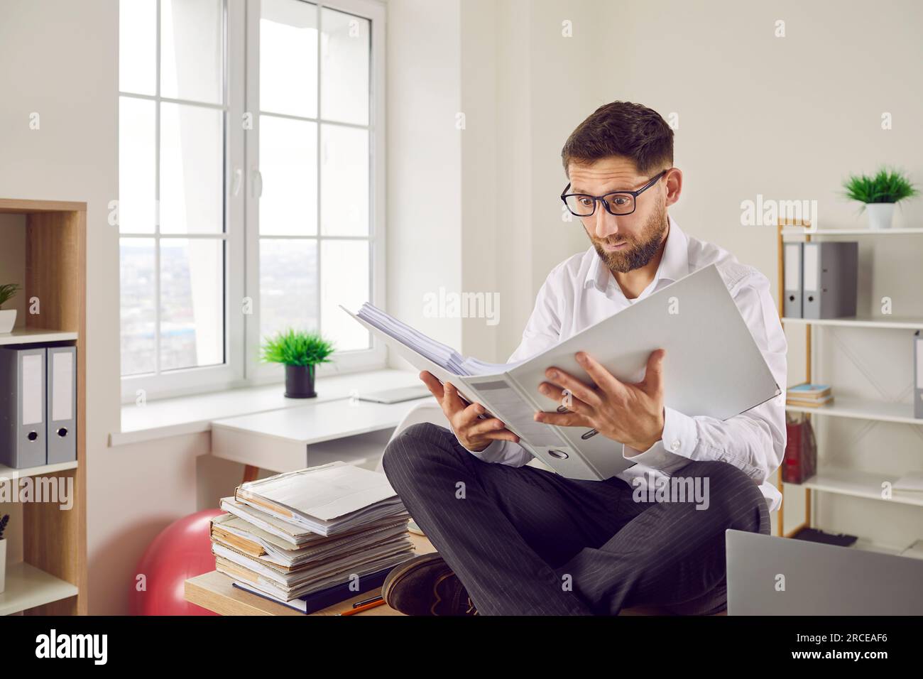 Funny, shocked, confused man sitting on his office desk and looking at ...