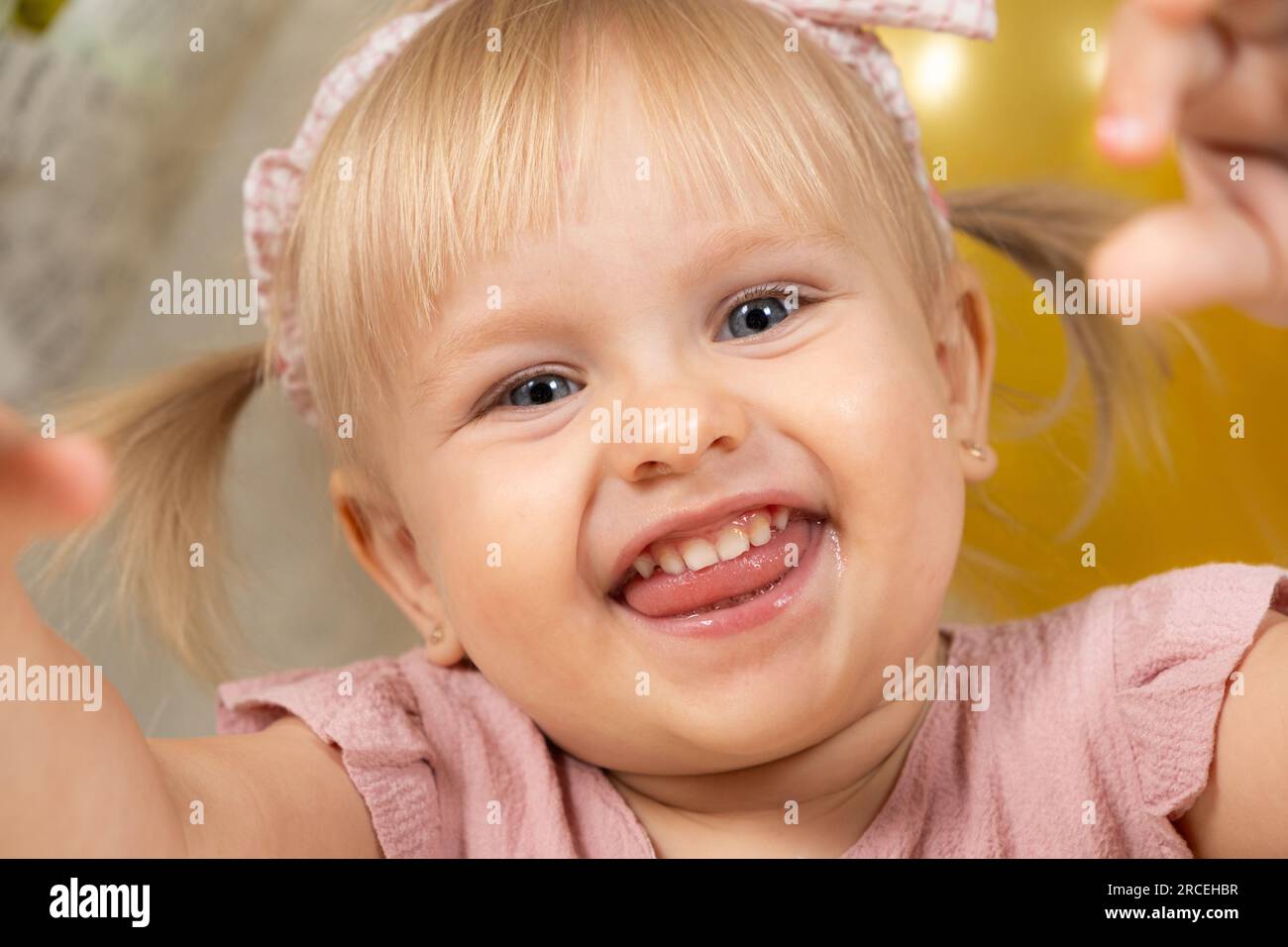 Two-year-old girl smiling looking at the camera, sticking out her ...