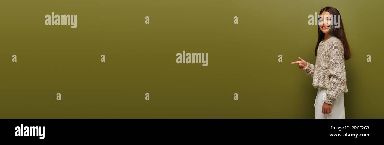 Cheerful preteen girl in modern cozy knitted sweater pointing with ...