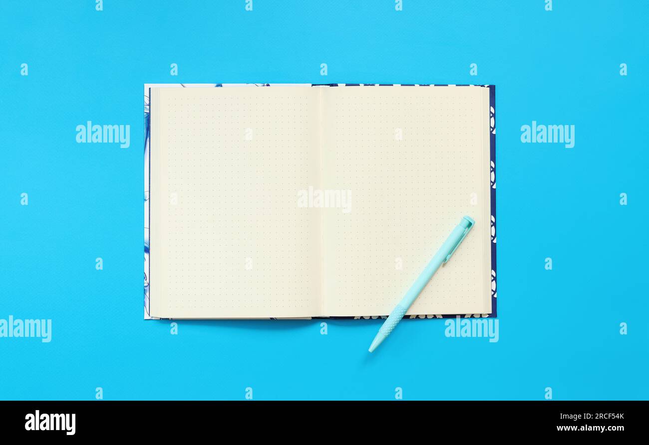 Mockup of an open notepad with a pen on a blue background. Top view ...