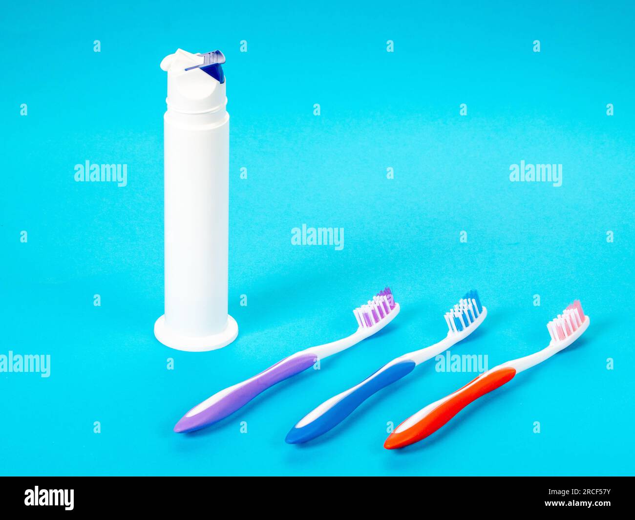 Three multi-colored toothbrushes and a tube of toothpaste on a blue ...