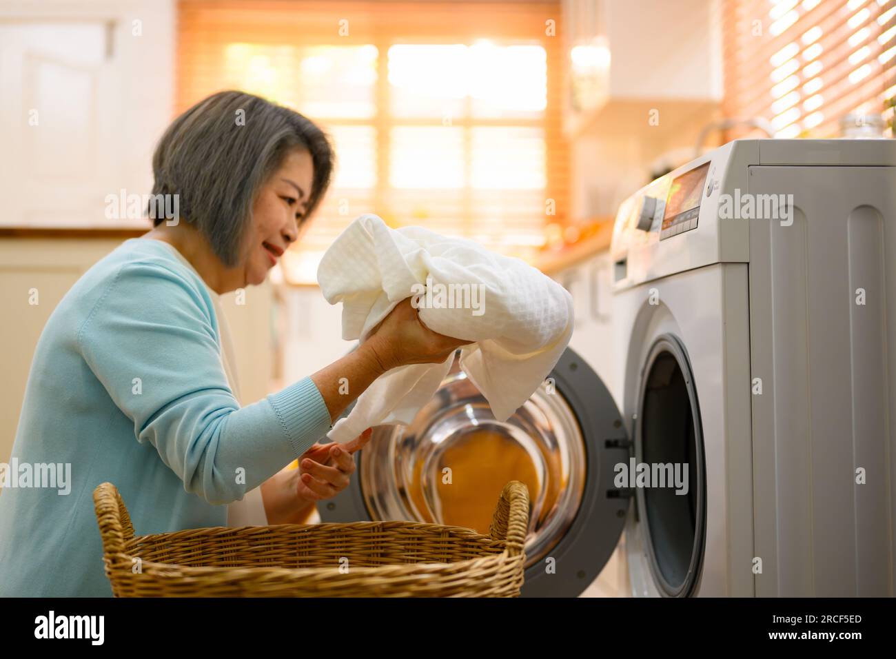 a beautiful senior woman, takes care of the laundry using a washing ...