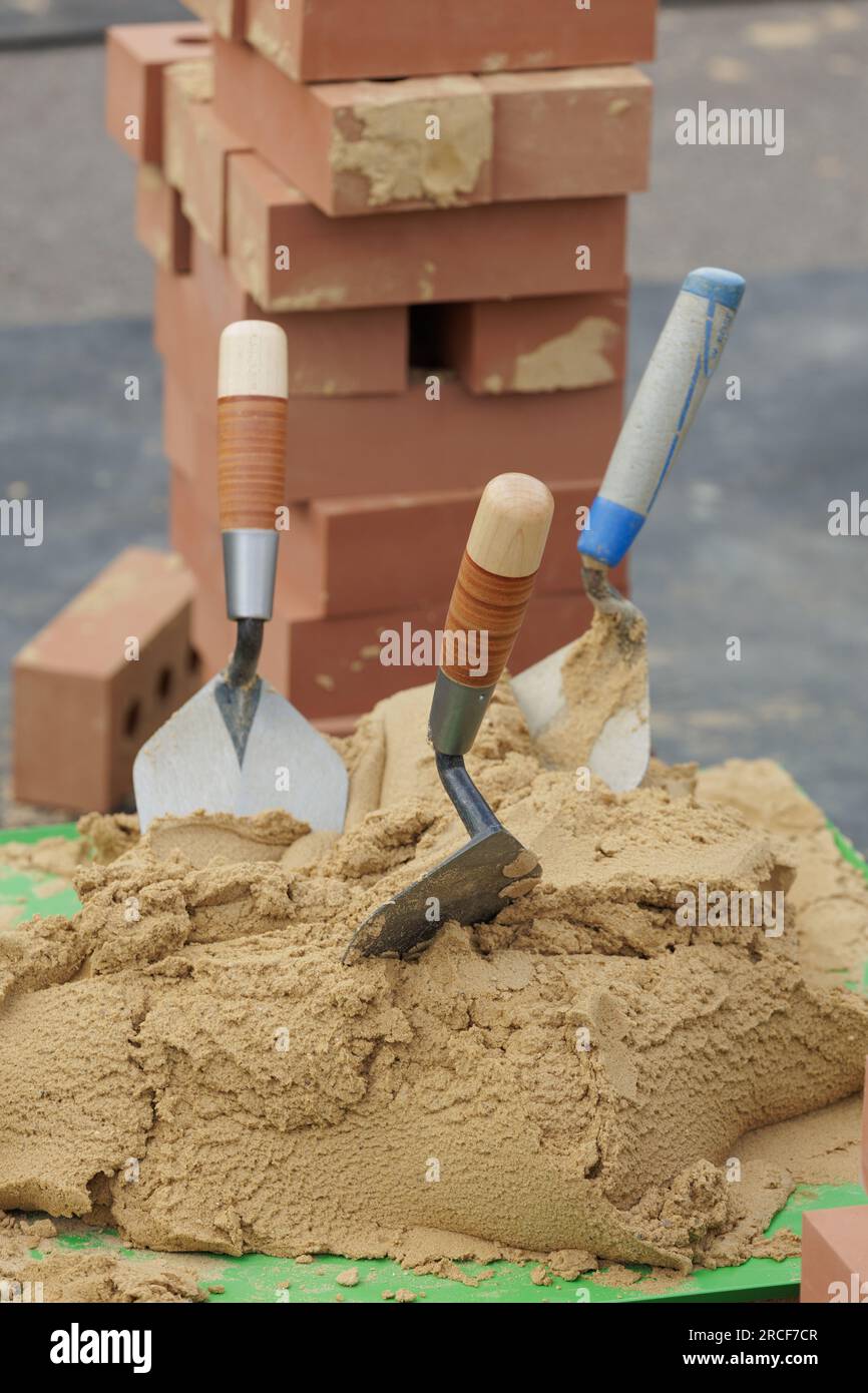 Three builders building trowels in pile of cement mortar, with stack of ...