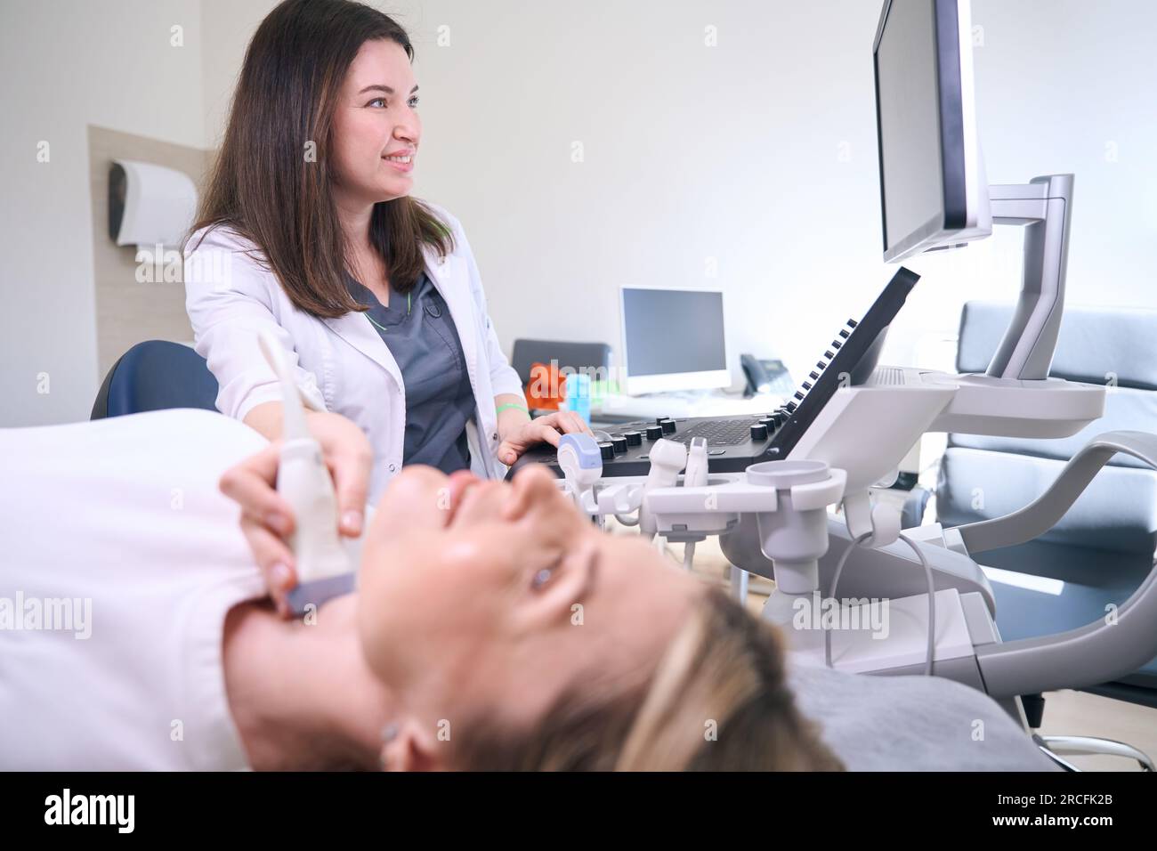 Pleasant female doctor conducts an ultrasound examination of thyroid ...