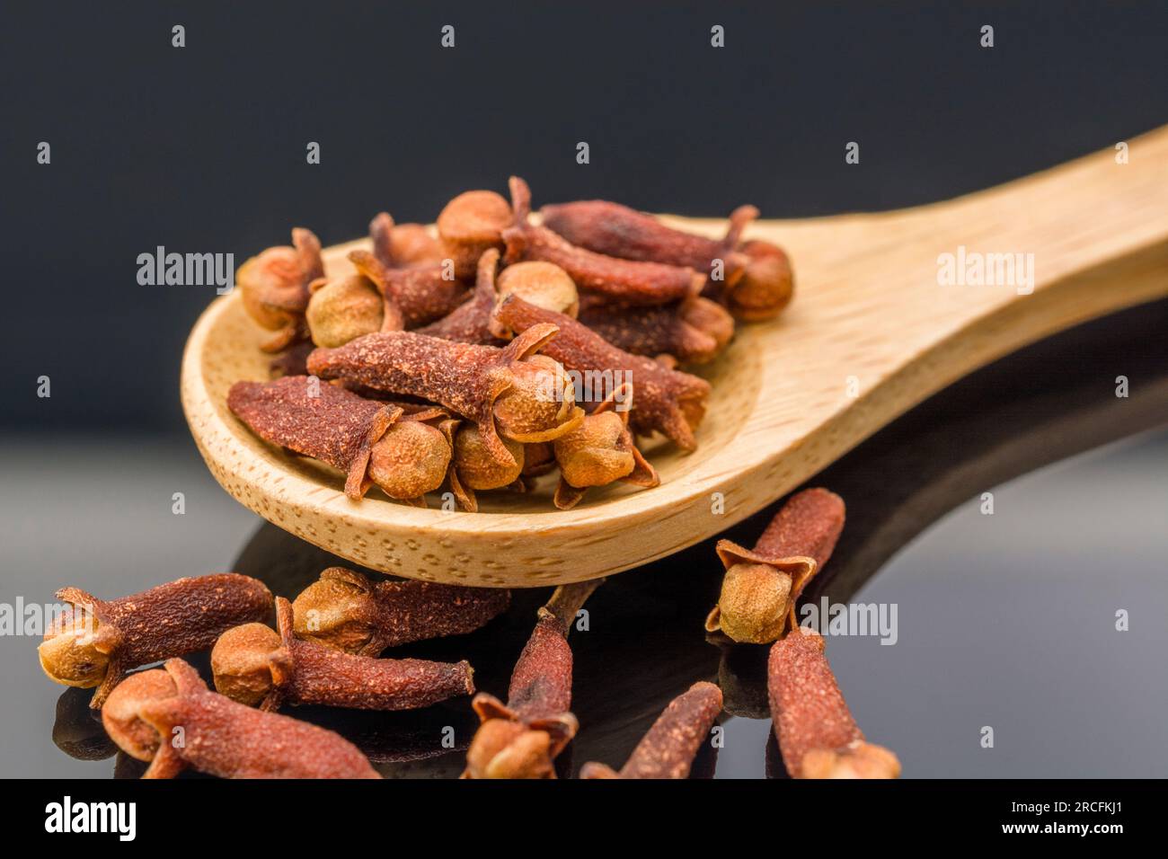 Dried Cloves / Syzygium aromaticum on small bamboo spoon on reflective black background. For ...