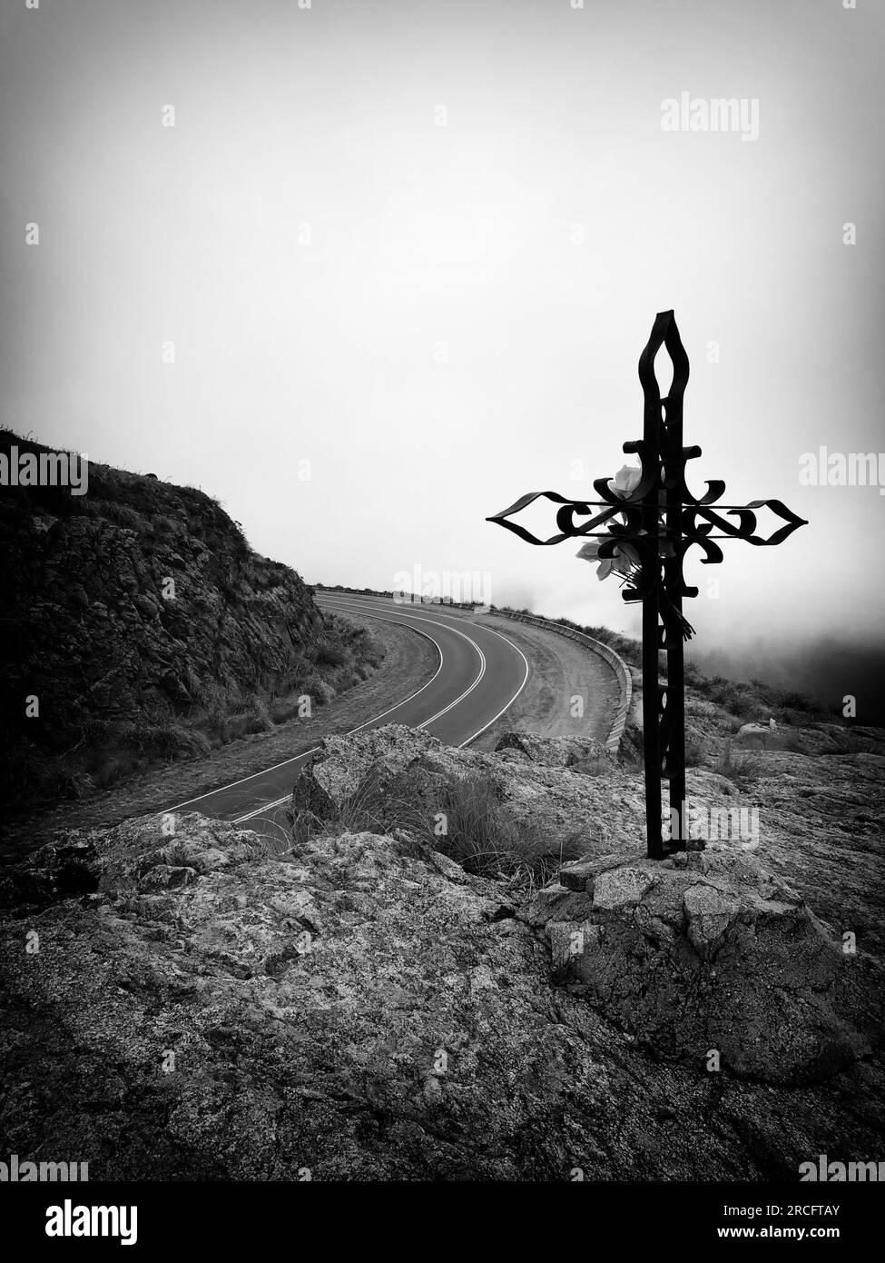 Cross on a rock overlooking the road in a mountainous area. Foggy sky ...