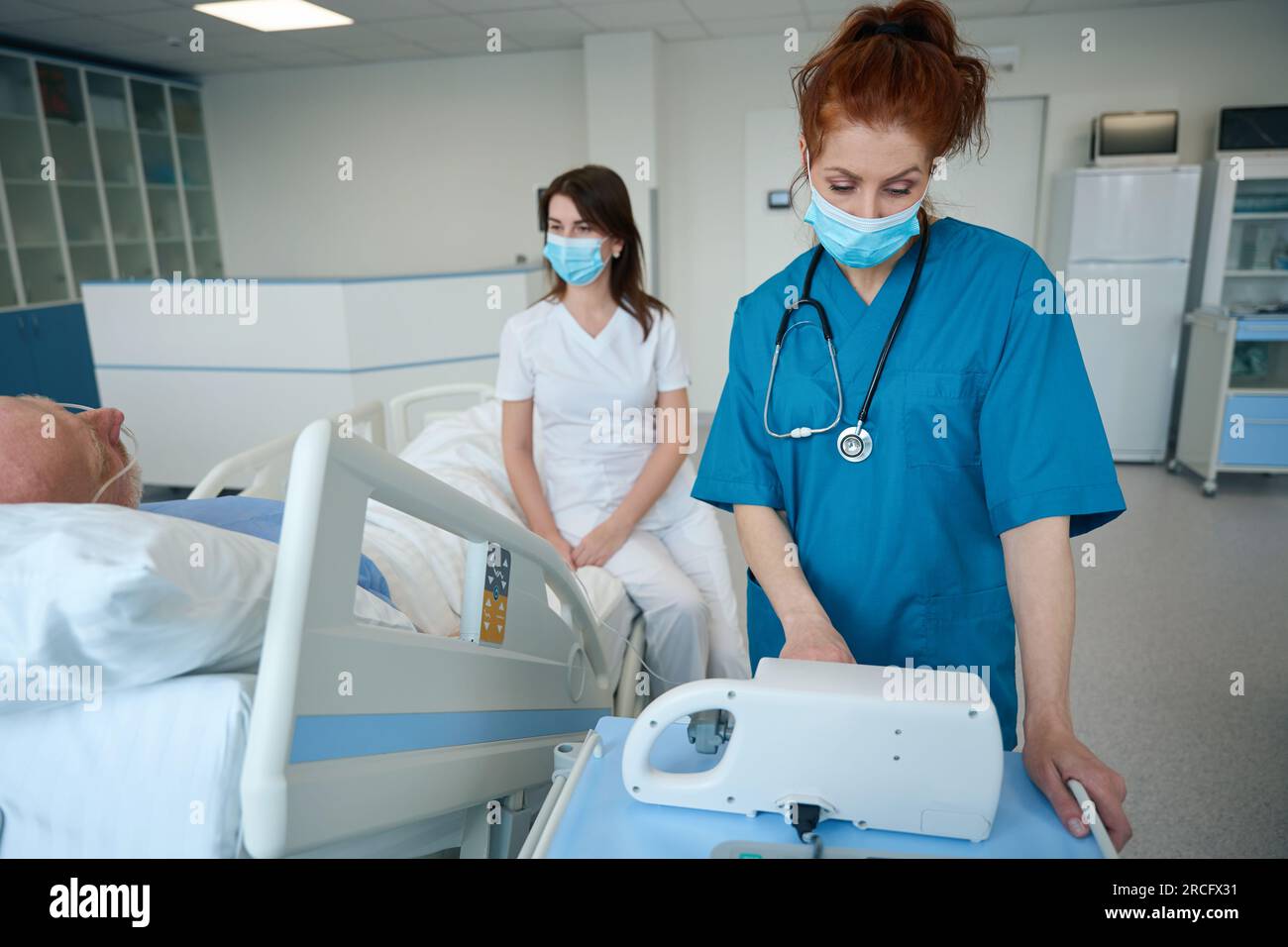 Nurse adjusting syringe pump and doctor near patient on bed in ...