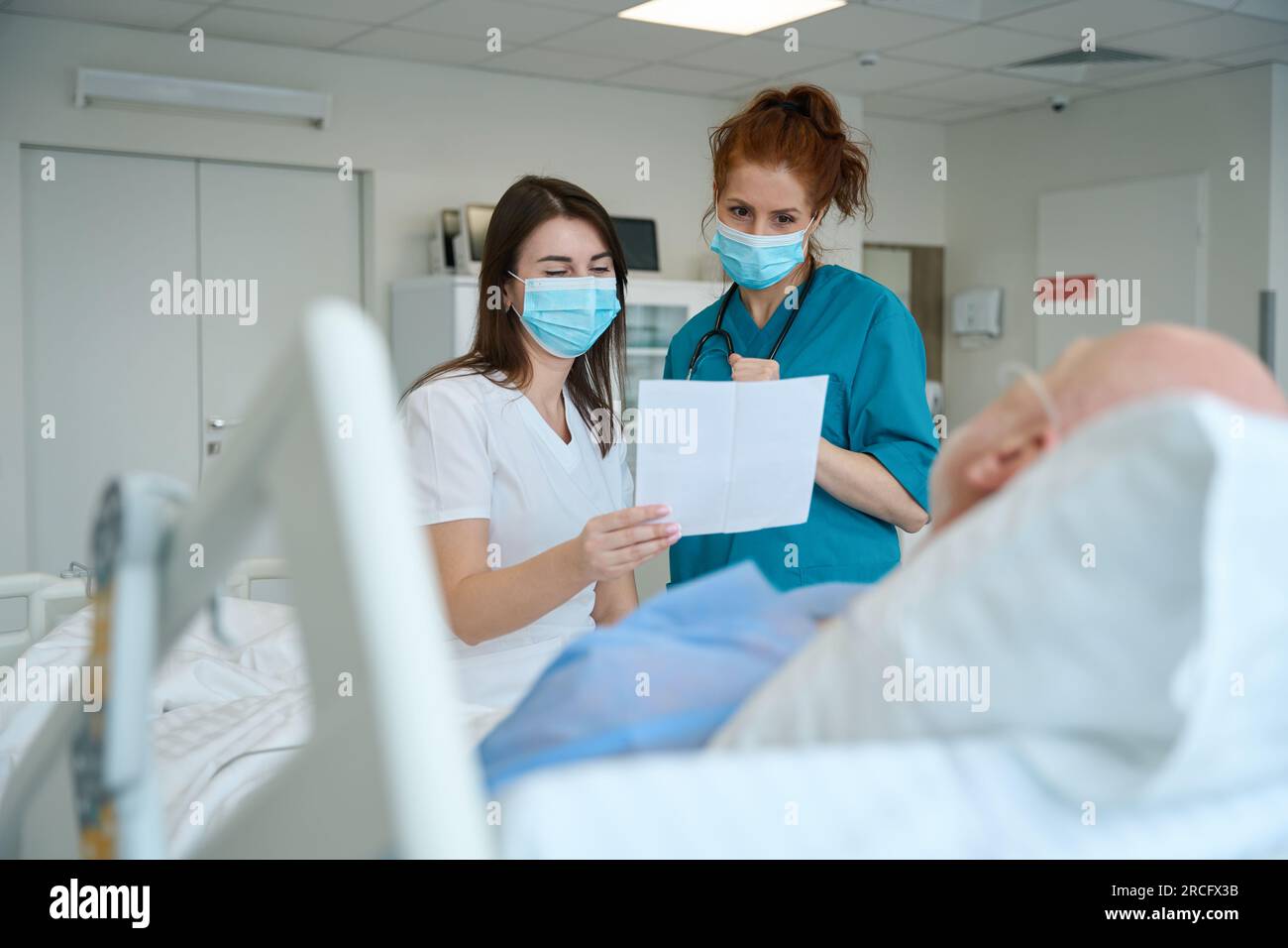 Female doctors with piece of paper visiting male patient in ward Stock ...