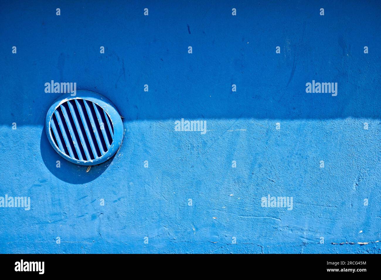 Round slatted vent port on an empty blue wall in two blue tones ...
