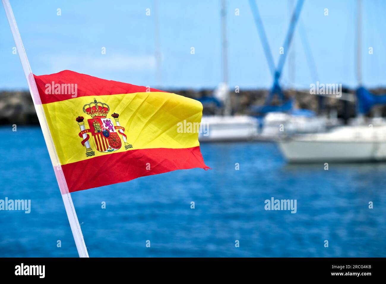 Spanish flag in the wind with sailing boats in a marina in a blurred ...