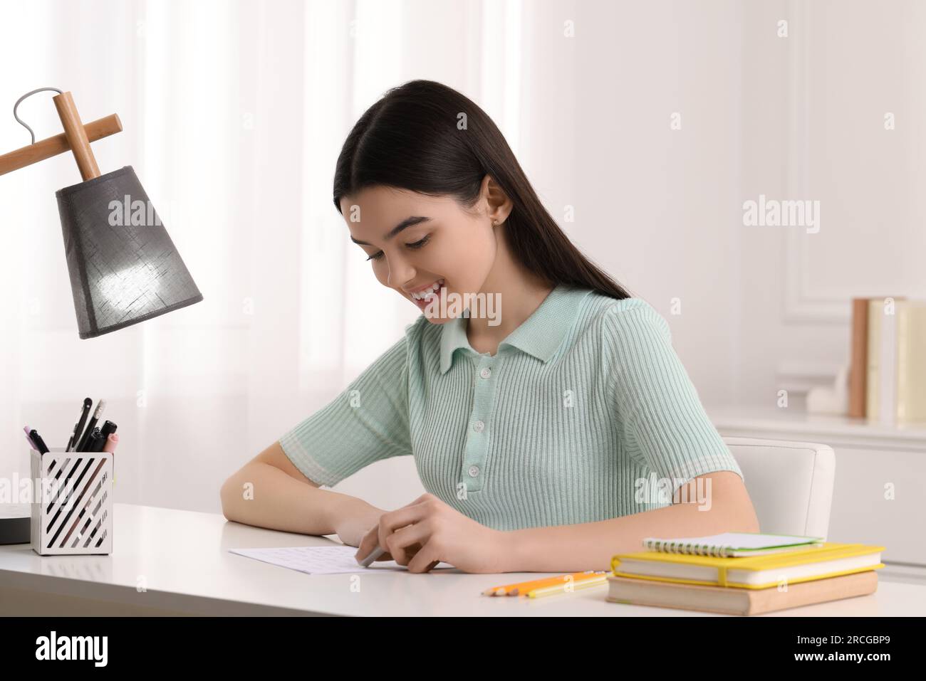 Teenage girl erasing mistake in her notebook at white desk indoors ...