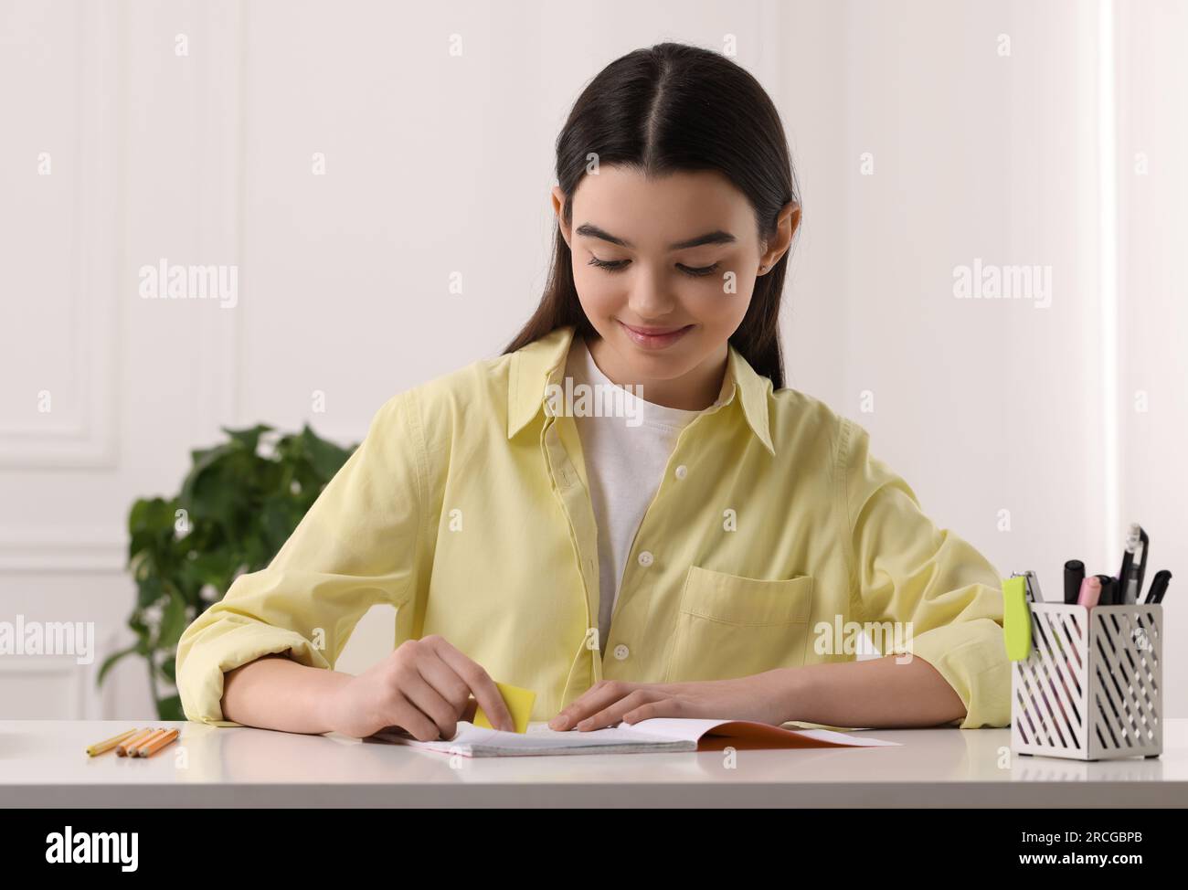 Teenage girl erasing mistake in her notebook at white desk indoors ...