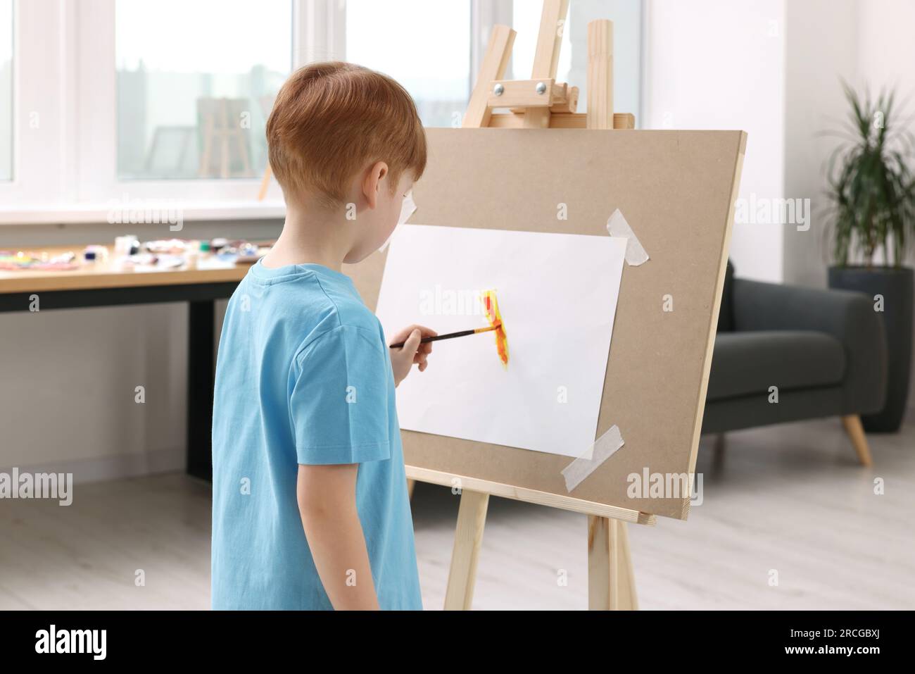 Little boy painting in studio, back view. Using easel to hold canvas ...